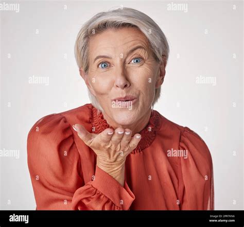 Une heureuse femme de race blanche mûre soufflant un baiser avec ses mains sur un fond gris