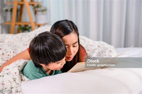 아시아의 어머니는 아들과 함께 집으로 일합니다 엄마와 아이는 침대에서 잠들기 전에 동화를 읽는다 여성의 라이프 스타일과 가족