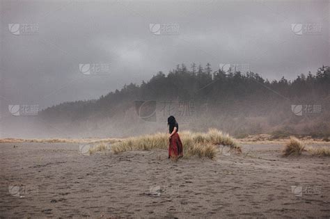 一个年轻的女人在一个多雾的海滩上，独自，女孩穿着格子裙和长发在海滩上