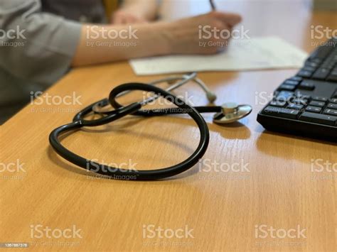 의학 저널에 글을 쓰는 여성 의사 치료사를 닫고 사무실에서 청진기가있는 테이블에 앉아 있습니다 건강관리와 의술에 대한 스톡 사진