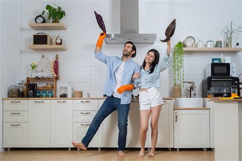 행복한 젊은 부부는 집안일을 하고 노래하고 재미있게 놀고 있습니다 집에서 부엌을 청소하는 동안 노래를 부르고 춤을 추는 재미있는 여자 25 29세에 대한 스톡 사진 및 기타