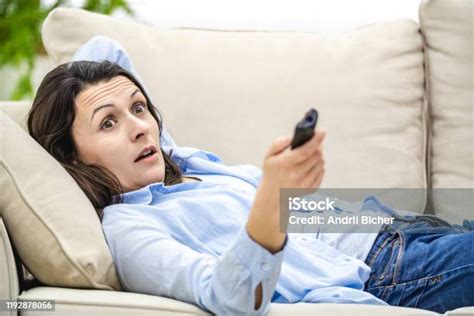 충격을 받고 놀란 여자는 소파에 누워 Tv를 보면서 그녀의 입을 엽니 다 자르기 닫아 Tv 보기에 대한 스톡 사진 및 기타