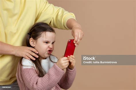 여자의 손 베이지 색 배경에서 멀리 스마트 폰을 복용 부모의 초상화 화가 난 딸은 꽉 전화를 잡고 저항합니다 어린이 의 전화