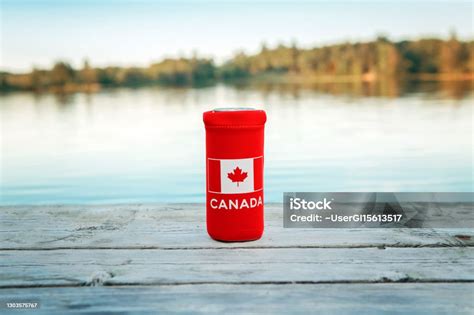 빨간 아늑한 맥주로 맥주 캔은 캐나다 국기가 야외 호수 옆에 있는 나무 부두에 서 있는 것을 식쌀 수 있습니다 7월 1일 캐나다의 날 전국 행사를 물 속 자연공원에서