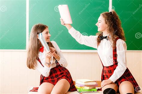 Two Beautiful Schoolgirls Are Sitting At The Desk With Books In The