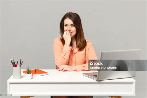 파스텔 캐주얼에 젊은 신경 여자 옆 갉 아 먹는 손톱을 찾고 회색 배경에 고립 된 Pc 노트북 책상에서 작업 앉아 성취 비즈니스 커리어 라이프 스타일 컨셉 복사 공간을 모의