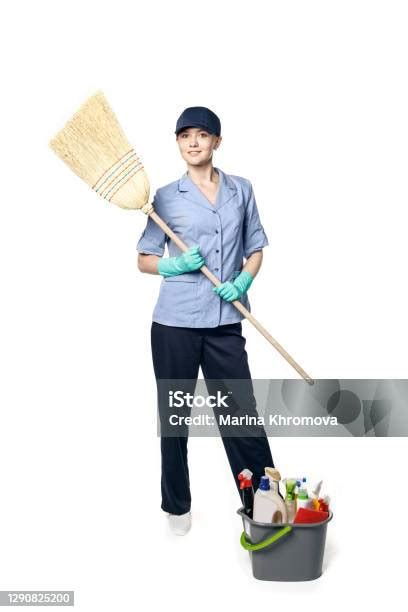 청소 여인과 야구 모자의 유니폼을 입은 소녀가 흰색 배경에 서 있습니다 그녀는 빗자루와 젖은 청소 제품이있는 플라스틱 바구니를 가지고 있습니다 가사 집안일에 대한 스톡 사진