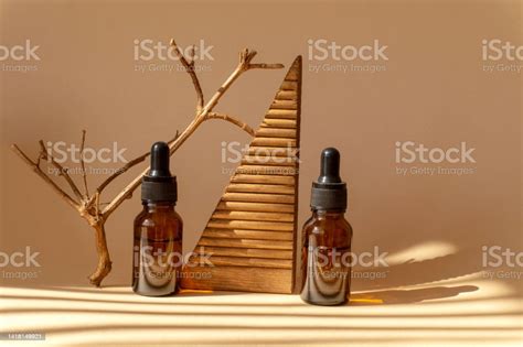 나무 기하학적 3d 연단의 배경에 얼굴 세럼이있는 두 개의 호박색 유리 병 화장품 용 점적기 뚜껑이있는 깨끗한 용기 모형 햇빛의