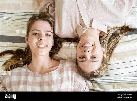 Two Cheerful Blond Teenage Girls Looking At You While Relaxing On Bed