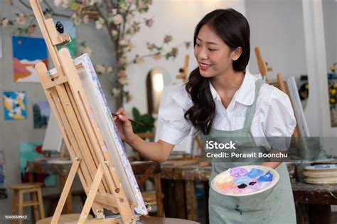 여자는 스튜디오에서 유성 물감으로 캔버스에 그림을 그린다 여성 예술가가 작업장에서 그림을 그린다 젊은 여성 예술가는 붓으로