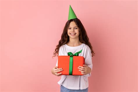 파티 콘에 빨간 포장 선물 상자를 들고 만족스러운 표정으로 카메라를 바라보는 어린 소녀 선물에 대한 스톡 사진 및 기타 이미지 선물 아이 대형 Istock