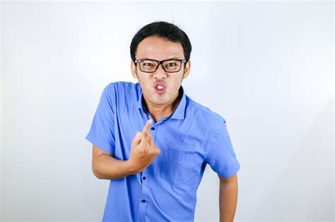 젊은 아시아 남자 입고 파란색 셔츠는 흰색 배경 위에 고립 된 카메라에서 소리지르고 손가락을 가리키는 재미있는 화가 얼굴입니다