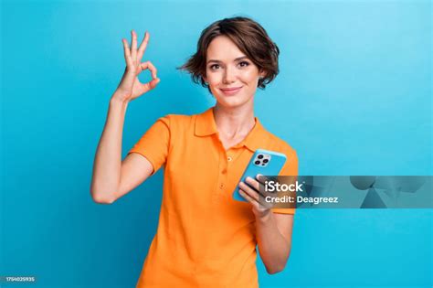 펑키 자신감 레이디 착용 오렌지 티셔츠 Okey 제스처 입력 Sms 현대 장치 절연 블루 컬러 배경을 보여주는 사진 전화에 대한
