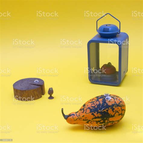 호박과 눈과 이상한 그림이있는 오래된 나무와 그 뒤에는 노란 배경에 촛불 대신 붉은 후추가있는 파란색 등불이 있습니다 미니멀 한 장면 10월에 대한 스톡 사진 및 기타