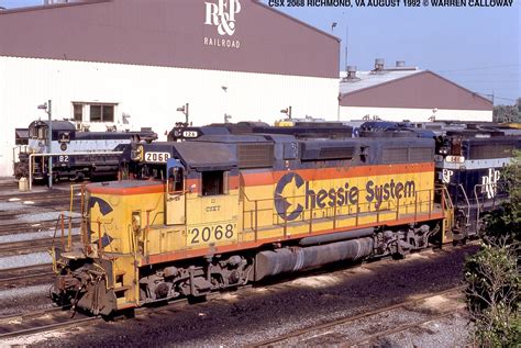 A Yellow And Orange Train Is On The Tracks Near A White Building With A