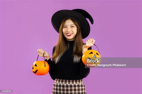 할로윈 테마 검은 색 의상을 입은 젊은 아시아 여성이 마녀 모자를 쓰고 웃고 보라색 등불에 호박 등불을 들고 있습니다 10월에 대한 스톡 사진 및 기타 이미지 Istock