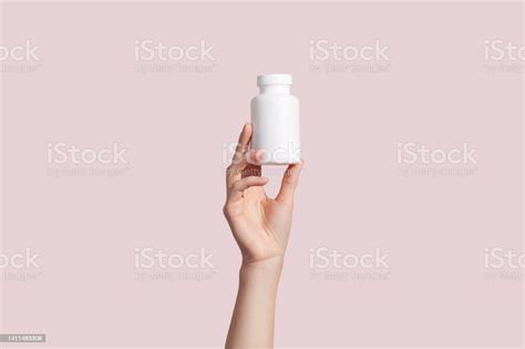 분홍색 배경에 빈 흰색 스퀴즈 병 플라스틱 튜브를 들고있는 젊은 여성 손 알약 캡슐 또는 보충제 포장 제품 브랜딩 모형 비타민에