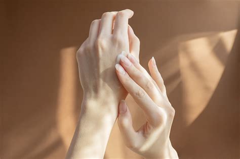 아름다운 여성의 손은 손바닥에 크림을 묻히고 로션을 피부에 바릅니다 클로즈업 줄무늬 그림자가있는 베이지 색 배경 손 관리의 개념
