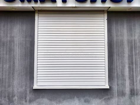 A White Rolling Shutter Is Closed Obstructing The Window Of A Building