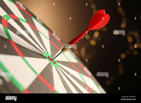 Red Arrow Hitting Target On Dart Board Against Black Background With Blurred Lights Closeup