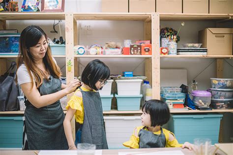 An 아시아의 예술 클래스 중국의 여성 선생 도움 하나의 그녀의 학생에 넥타이 올라 그녀의 앞치마 시작 하기 전에 예술 수업 그리기 활동 교사 교육 관련 직업에 대한 스톡