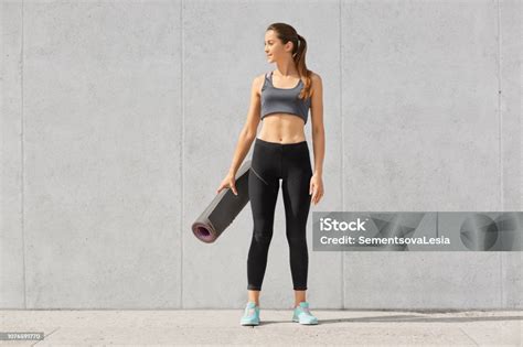 전체 길이 총 인의 슬림 피트 니스 시체 착용 탑 레 깅 스와 운동 화 운동 매트 체육관에서 운동을 해야 할 것은 회색 콘크리트 벽에 포즈 보유 하고있다 신중 하 게 옆으로