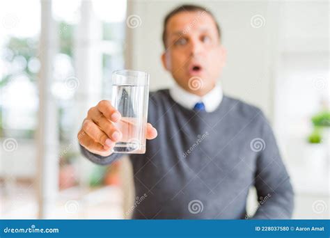 Middle Age Man Drinking Glass Of Water At Home Scared In Shock With A