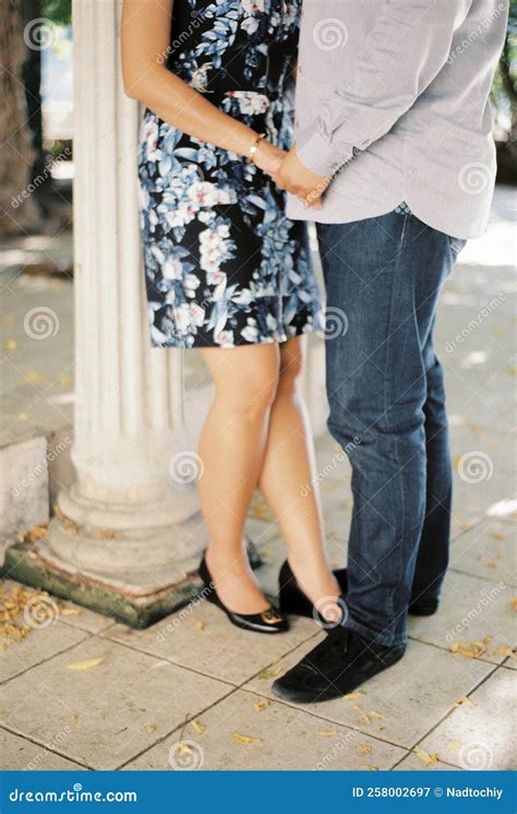 Man Holds Woman By The Hands While Standing Near A Column Cropped