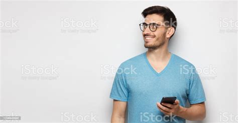 파란색 티셔츠와 안경을 쓰고 스마트폰을 손에 들고 서서 회색 배경에 고립된 공간을 복사하고자 하는 젊은 잘생긴 남자의 수평 배너 20 29세에 대한 스톡 사진 및 기타