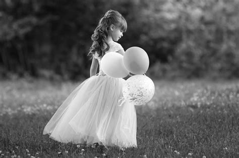 검은 색과 흰색 프로필 흐린 배경에 피는 필드에 서 공기 풍선 긴 흰색 드레스꽤 작은 금발 긴 머리 소녀의 전체 길이 초상화