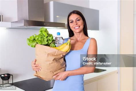 부엌에 서있는 채소와 식료품 쇼핑 백을 들고 젊은 여자 집에서 부엌에서 야채와 식료품 쇼핑 백을 들고 행복한 여자 가방에 대한