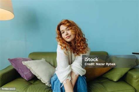 Wanita Muda Ceria Yang Cantik Duduk Di Sofa Di Ruangan Berwarna Biru