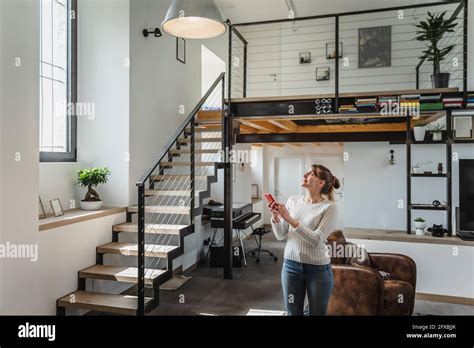 Young Woman Controlling Smart Home Functions Through Mobile Phone At