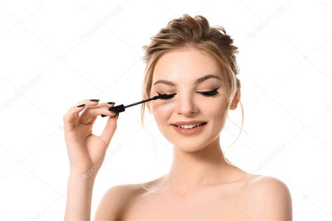 sonriente mujer rubia hermosa desnuda con maquillaje y uñas negras aplicando rímel aislado en