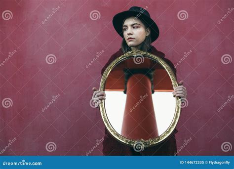 Young Teen Girl In Hat Holding Mirror In Front Of Red Wall The Mirror