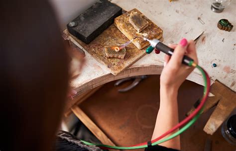 납땜 보석 및 액세서리 귀걸이 또는 반지에 대한 작업장의 여성 디자인 모양 및 수리를 위해 손에 용접 토치가 있는 보석상 직장에서 스타트 업 디자이너와 창조적 인 사업가