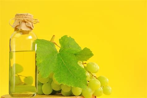 포도 씨 오일 마사지를 위한 베이스 오일과 얼굴과 몸을 케어합니다 밝은 노란색 배경에 병과 녹색 포도의 무리 유기농 천연 바이오