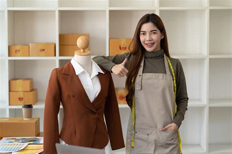 마네킹 근처에 서 있는 측정 테이프가 달린 펜시브 우먼 재봉사의 측면 보기는 모던 아틀리에에 새로운 패션 드레스를 바느질합니다