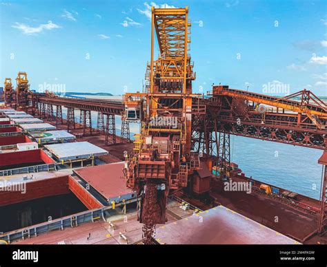 An Iron Ore Conveyor Loading Cargo In The Bulk Carrier With A Cloudy Blue Sky In The Background