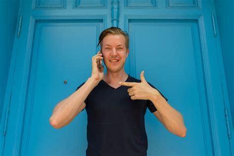 Hombre guapo joven feliz hablando por teléfono móvil y señalando con el dedo delante de la