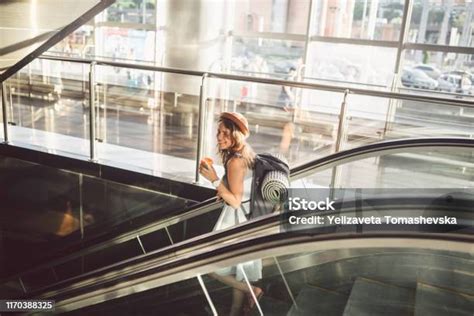 에스컬레이터에서 공항에서 모자를 쓰고 웃는 모습 기내 수하물을 가지고 여행하는 사람들 테마 관광 및 교통 에스컬레이터에 공항 터미널에서 커피와 백인 소녀 가방에 대한 스톡