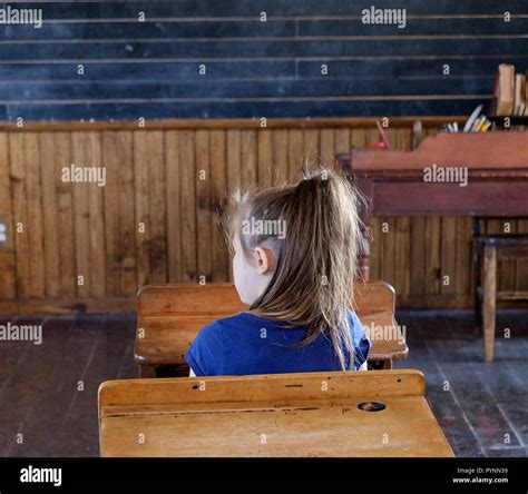 School Girl In Blue Top Sits At Vintage Wooden Desk In Classroom