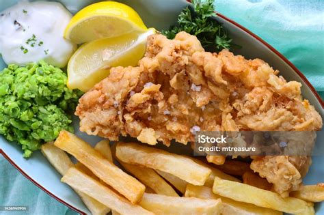 소금으로 맛을 낸 피쉬 앤 칩스의 전체 프레임 이미지 타원형 오리 달걀 파란색 접시 레몬 슬라이스 타르타르 소스 부드러운 완두콩