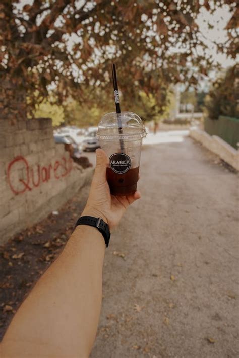 푸른 도시 거리에서 아이스 커피를 들고 있는 손 · 무료 스톡 사진