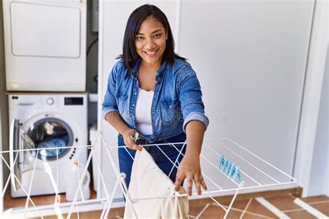 Hispanic Brunette Woman Hanging Clean Laundry On Rack At Laundry Room