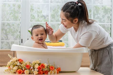 욕조에서 목욕하는 차분한 아시아 아기는 웃음을 즐깁니다 따뜻한 물에 아들을 목욕시키는 어머니 욕조에서 행복한 사랑스러운 신생아