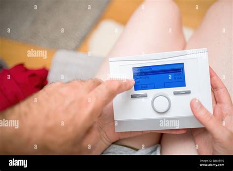 Woman And Malenmhands Interacting Holding New Digital Connected Thermostat With Menu Showing