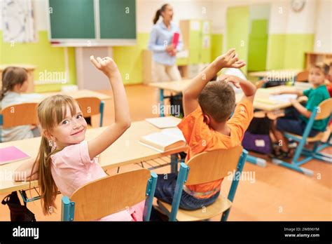 Smiling Schoolgirl Looking Away With Hand Raised During Lecture In