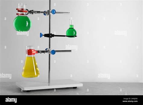 Retort Stand And Laboratory Flasks With Liquids On Grey Table Against