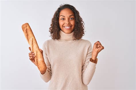 고립된 흰색 배경 위에 빵을 들고 있는 젊은 브라질 제빵사 여성이 자랑스럽고 승리와 성공을 축하하며 매우 흥분하고 환호하는 감정을 표현합니다 감정에 대한 스톡 사진 및 기타